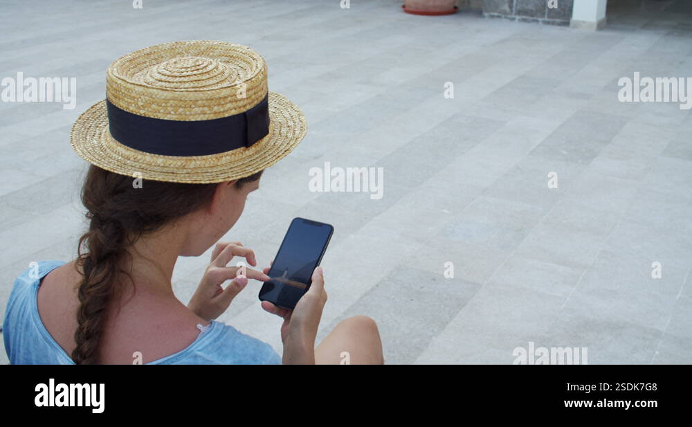 A woman tourist in a hat sits on a bench and looks at photos on a ...
