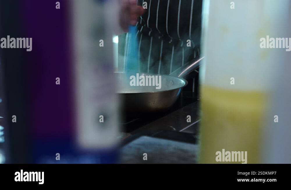 A man in a restaurant kitchen stirring a dish in a frying pan, steam ...