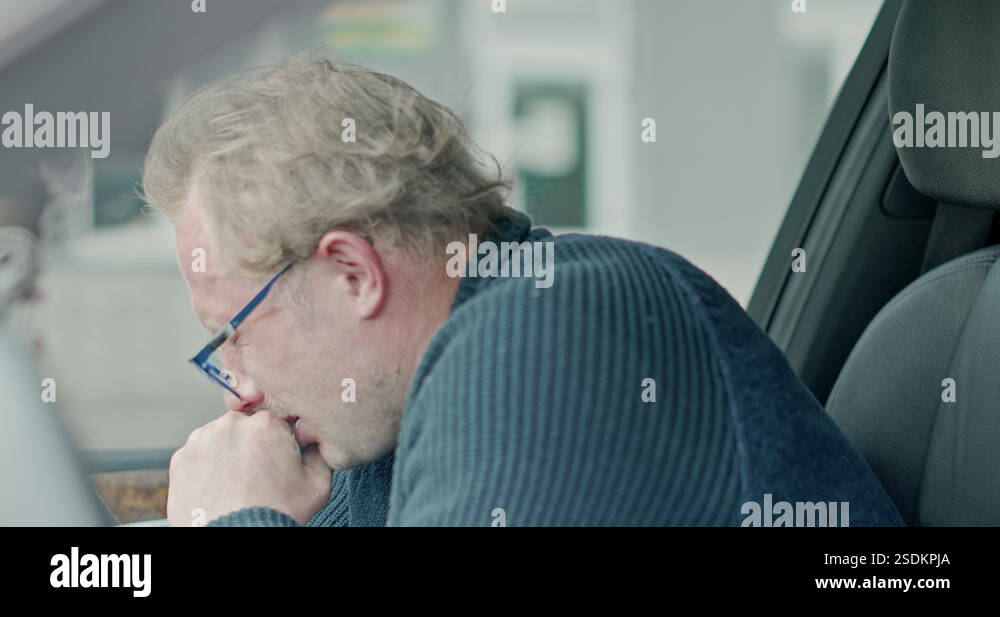 Man seated in a car taking a puff on a cigarette then coughing before ...