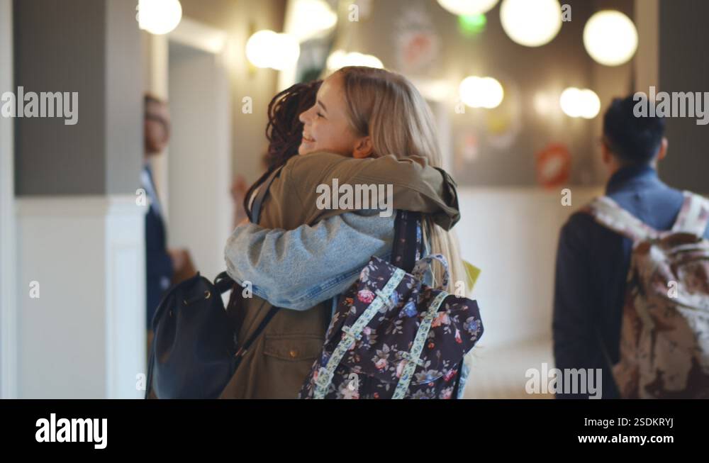 Two diverse female college classmates meeting and hugging in school ...