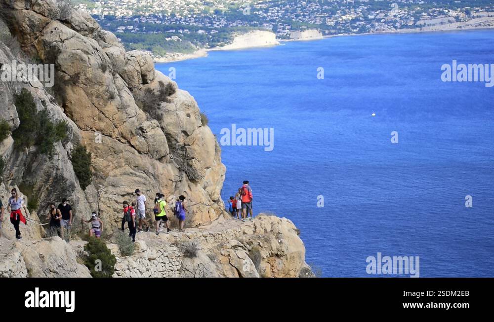 Crowd walk by the narrow path ascending to the Penon of ifach in Calpe ...