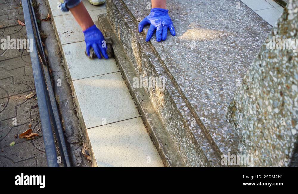 Cleaning cemetery. A woman washes grey paving slabs and monument grave ...