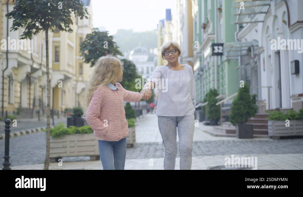 Joyful little girl pulling hand of smiling senior woman and leaving ...