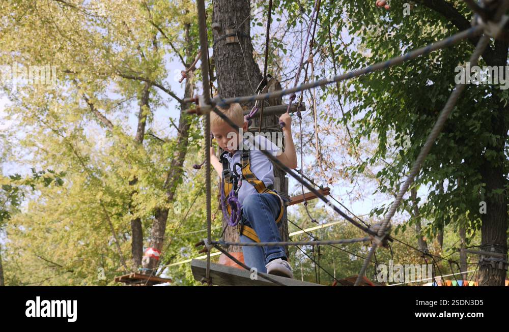 Cute school boy enjoying a sunny day in a climbing adventure activity ...