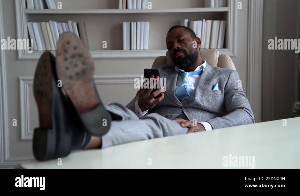 boring rich man is sitting in his office, lying legs on table, using ...