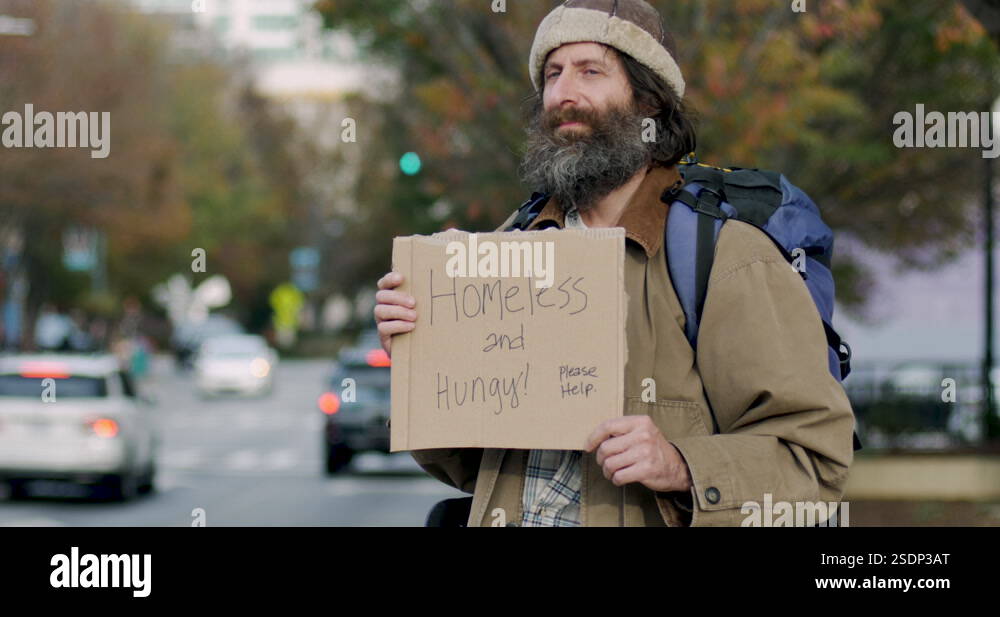 Man with a beard holding a homeless and hungry sign while standing on ...