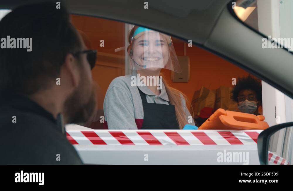Man driver in car ordering takeaway meal at drive thru counter of fast ...