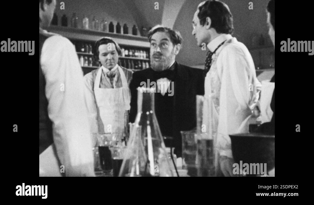 1950s: Men in aprons stand around scientist at laboratory table and ...