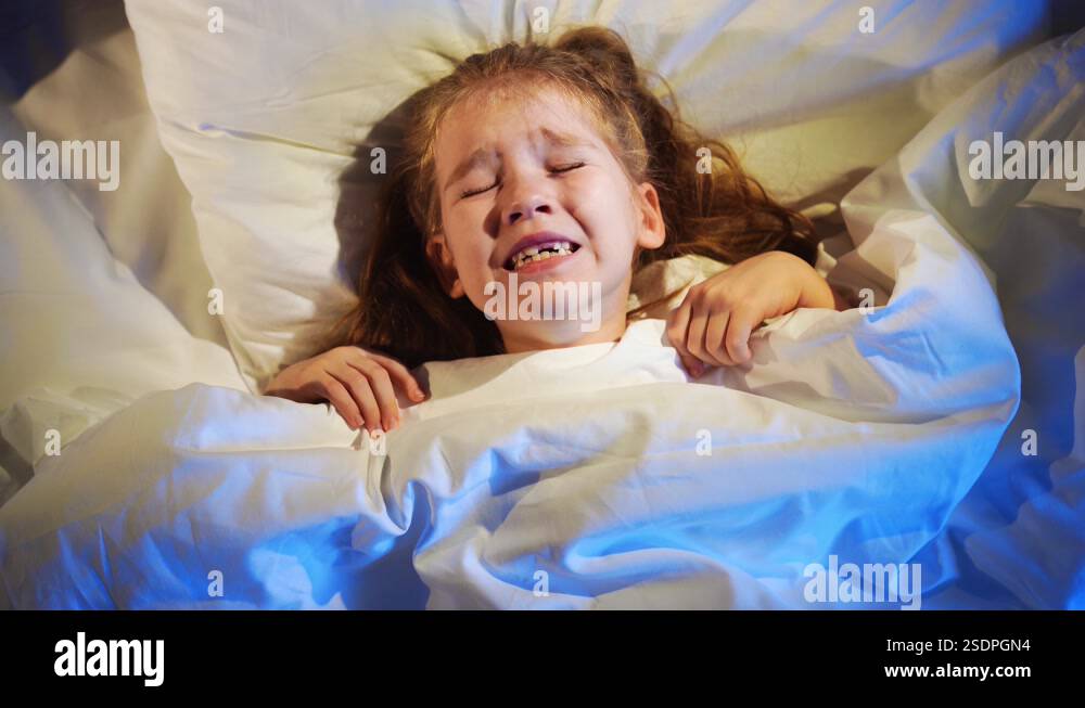 top view. A sweet little girl naps in bed, sees a nightmare and fears ...