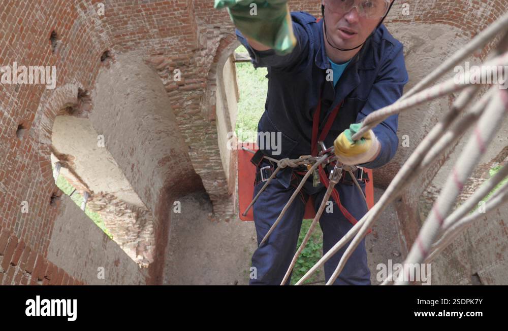 An industrial climber, suspended by ropes, descends the wall of a ...