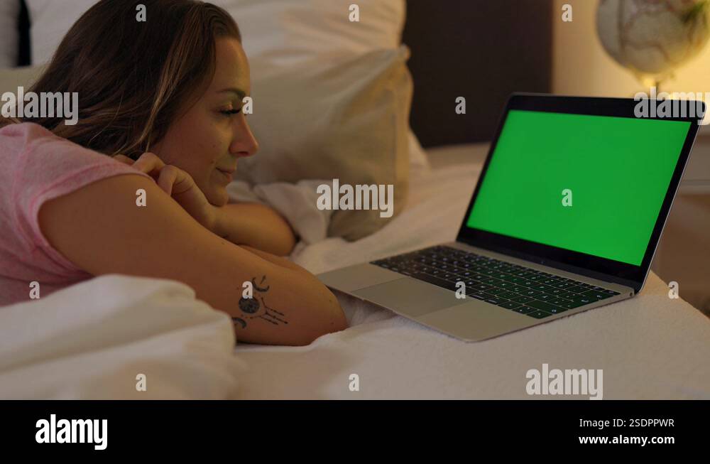 Young woman lies on the bed with her laptop - green screen display ...