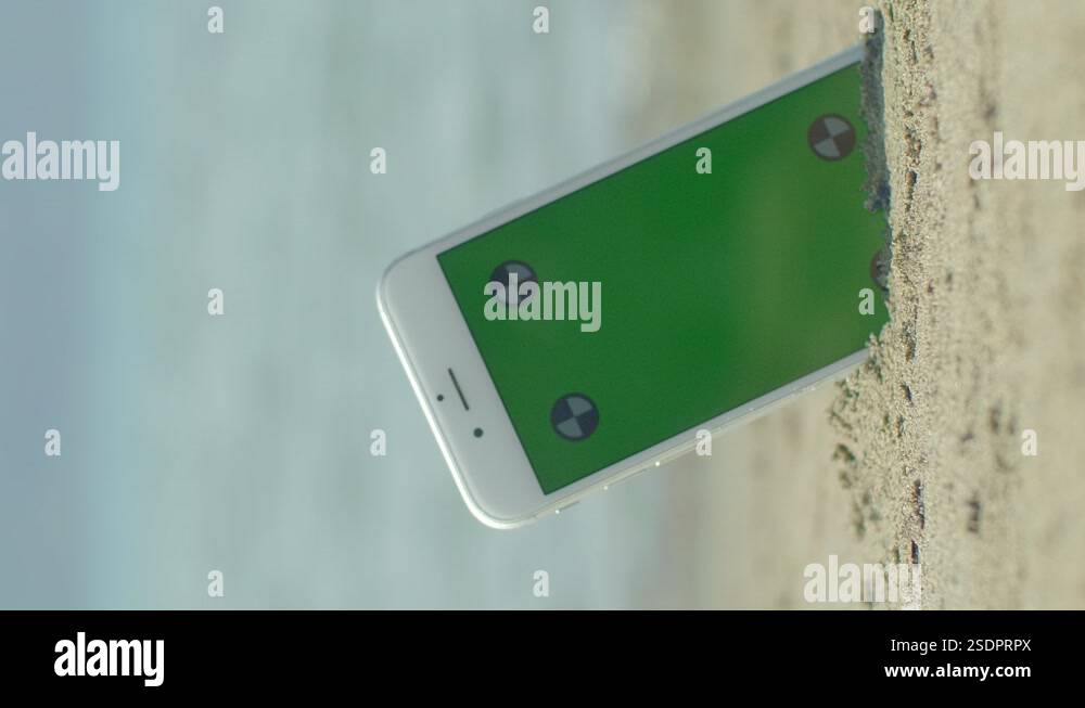 Mobile phone in sand at beach with green screen, sea and tracking signs ...
