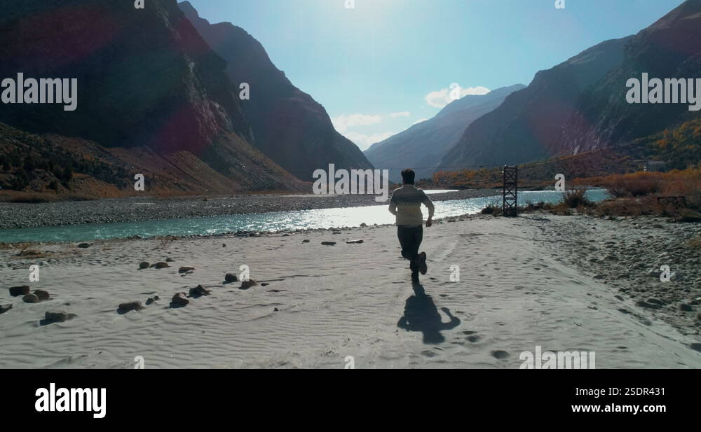 Back view of a solo traveler freely running in a mountain valley ...