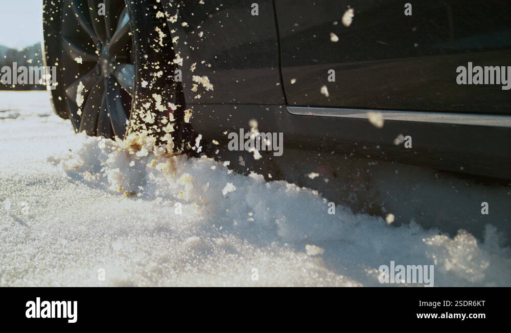 LOW ANGLE: A car's wheels spin and spit up snow as unknown driver tries ...