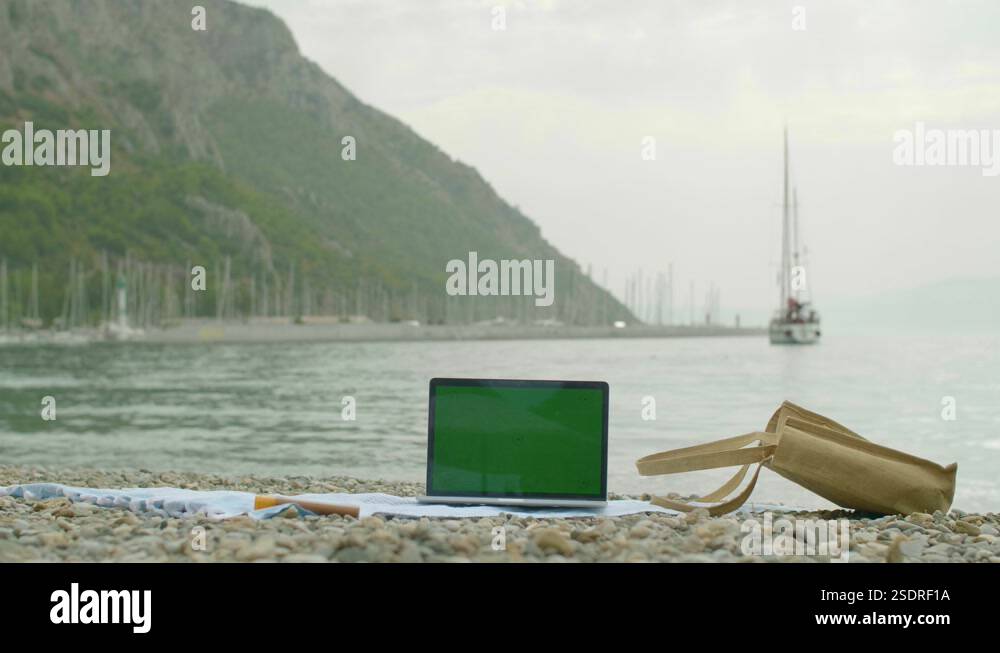 Straw beach bag, towel, sunscreen and computer with green screen on the ...