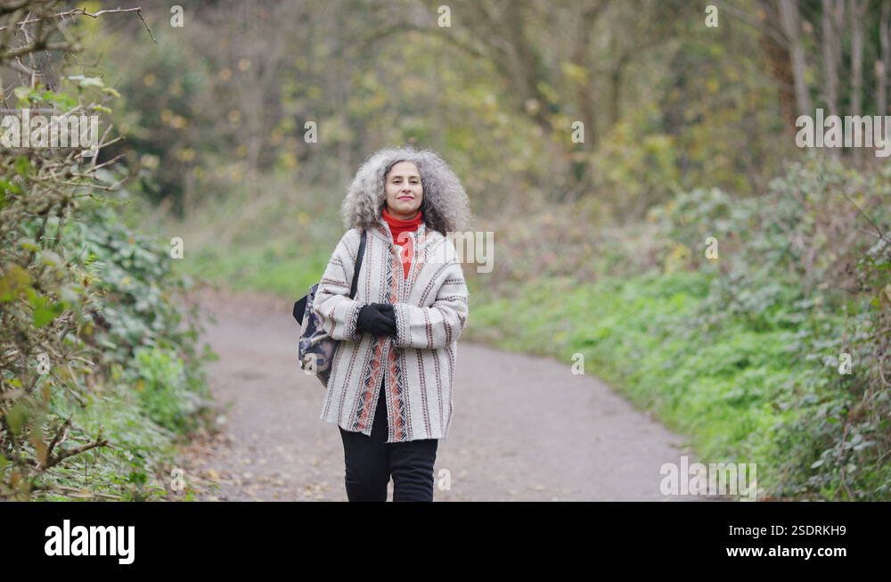 Attractive older lady walks by herself along a country path, in slow ...