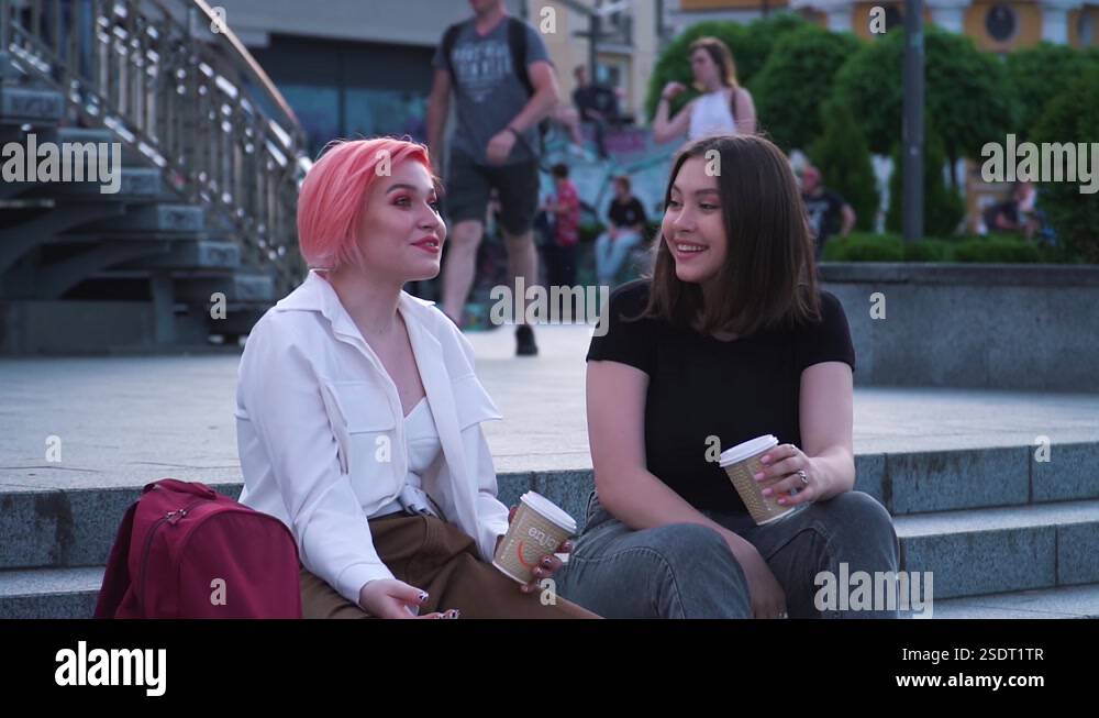 Two young women talking and laughing sitting on the granite stairs and ...