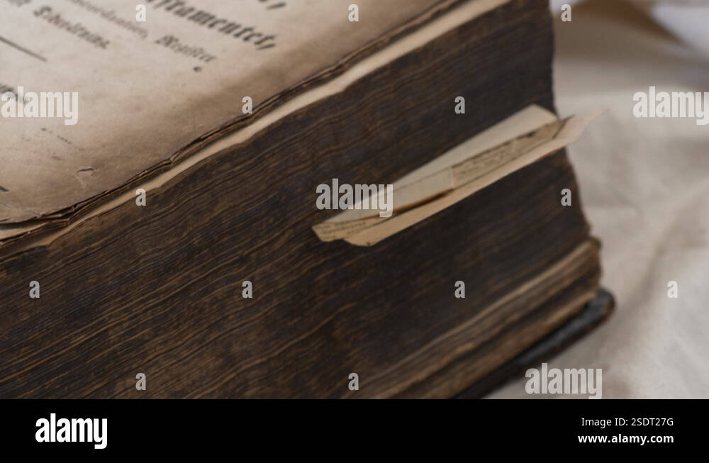 Close pan along ancient heavy worn bible in Swedish on white sheet ...