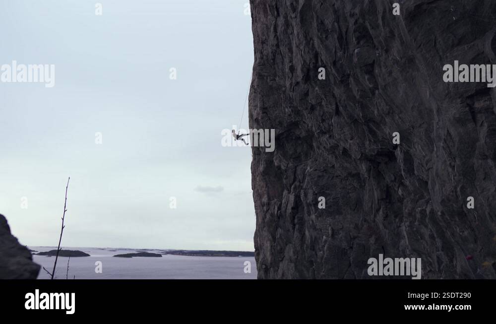 Man rappelling down a vertical mountain, ocean view in background Stock ...