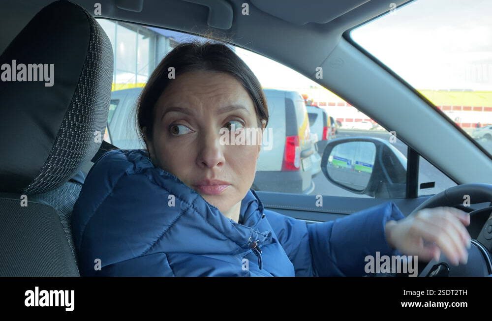 Woman driver driving car back into parking spot in the open parking lot ...