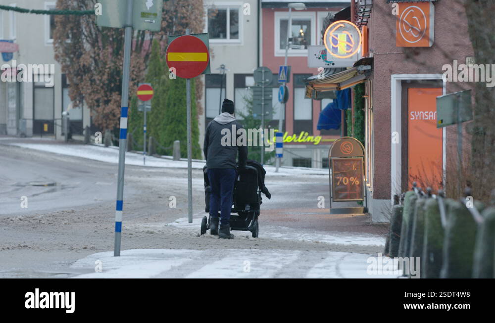 A man with a stroller, pram walks down a slush covered street in a ...