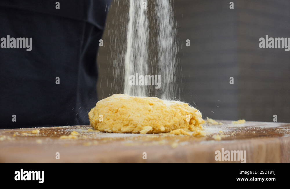 Sifting flour on dough on kitchen table while kneading. Chef is making ...