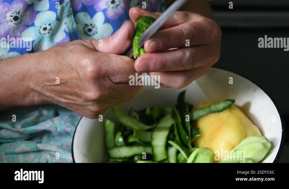 Closeup cutting cucumber peels with knife in wrinkled hands of senior ...