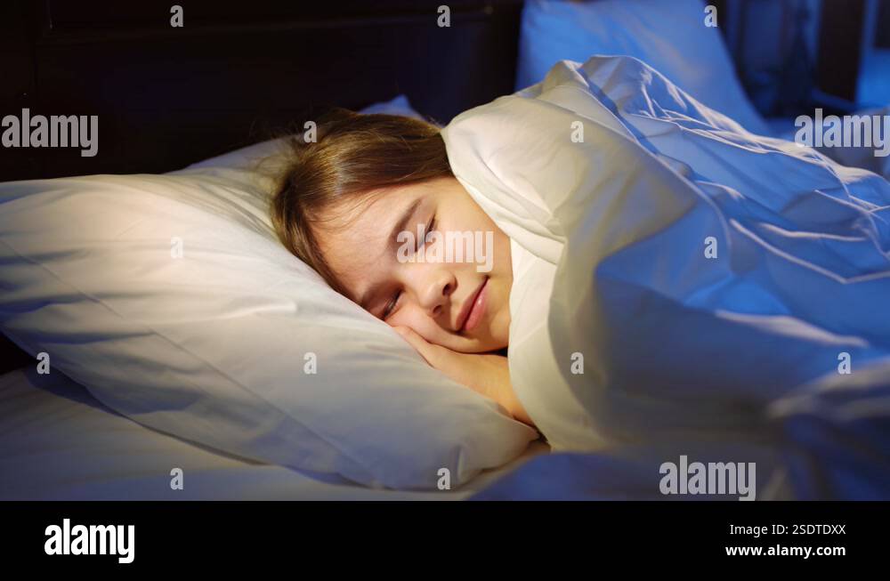The pretty teenage girl naps in bed, sees a pleasant sleep and smiles ...