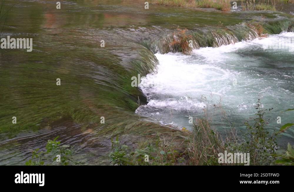 Close up of a strong current of water flowing from one pond down to ...