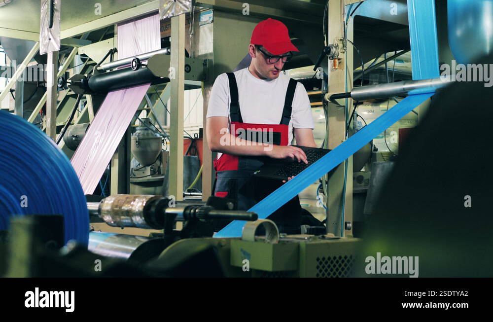 Male factory worker monitoring plastic bag production process with his ...