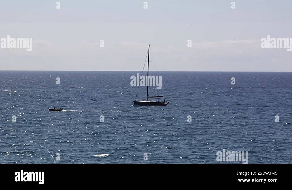 sailboat lulled by the waves with dinghy moving away on the horizon ...