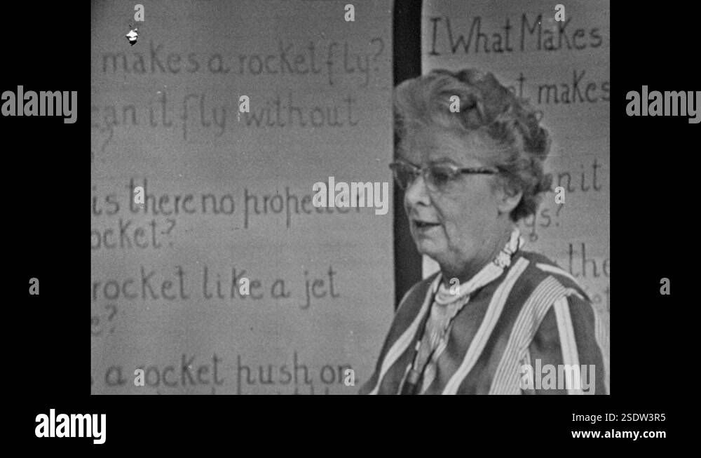 1960s: Woman sits in back of class, smiles. Teacher stands at front of ...