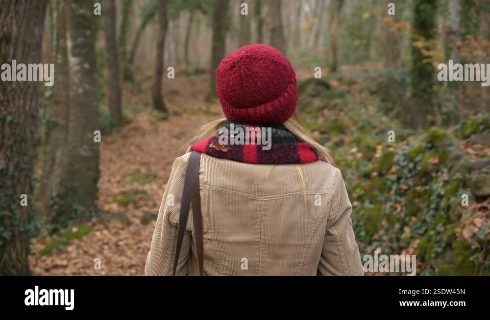 Following behind woman in red hat walking on path in autumn forest ...