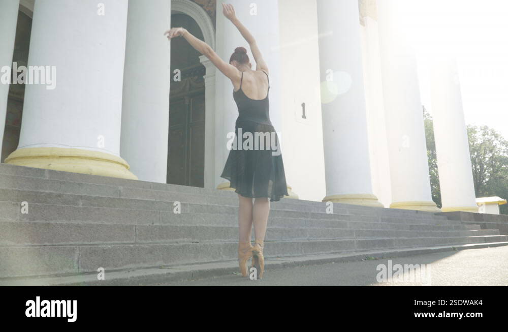 Back view of slim ballet dancer on tiptoes dancing in sunrays outdoors ...