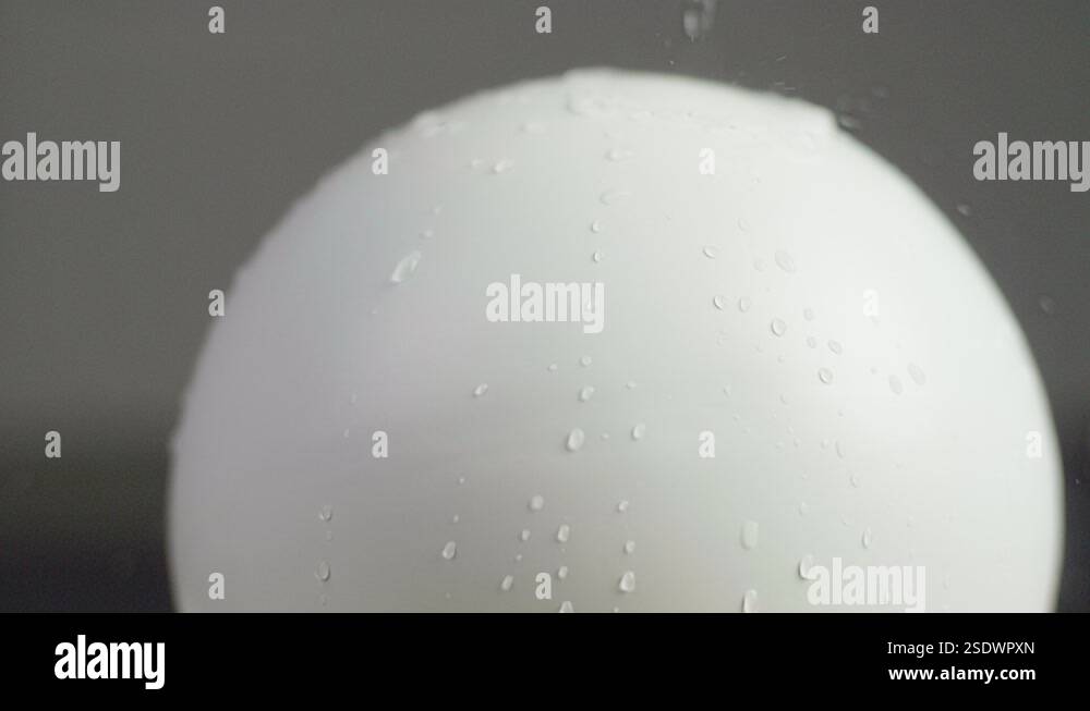 Close up of water falling on a plain white sphere with water srops on ...