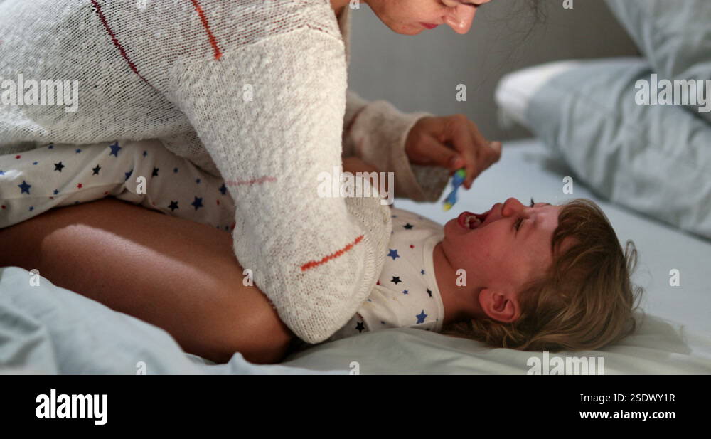 Candid mother brushing crying baby teeh. Upset infant boy not wanting ...