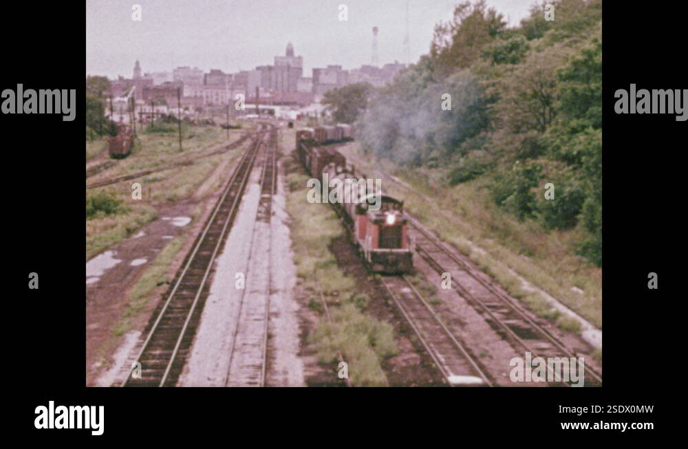 1970s: Train on railroad tracks. Crane on dock. Bridge with city behind ...