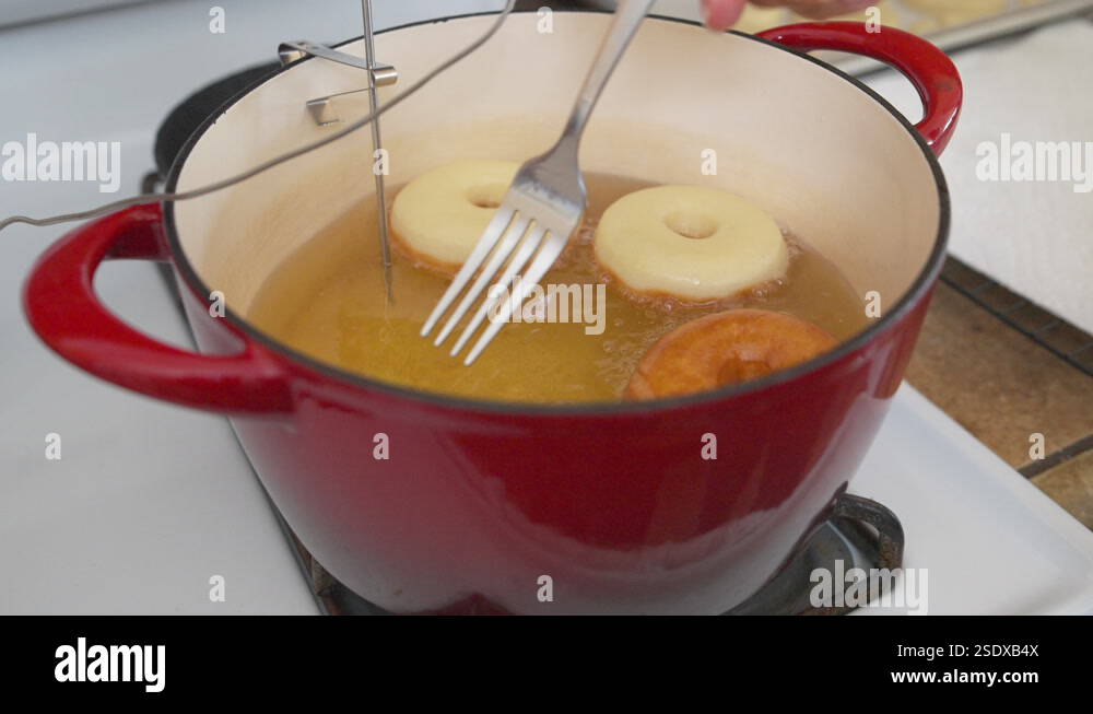 Flipping half fried donuts with fork while deep frying in dutch oven ...