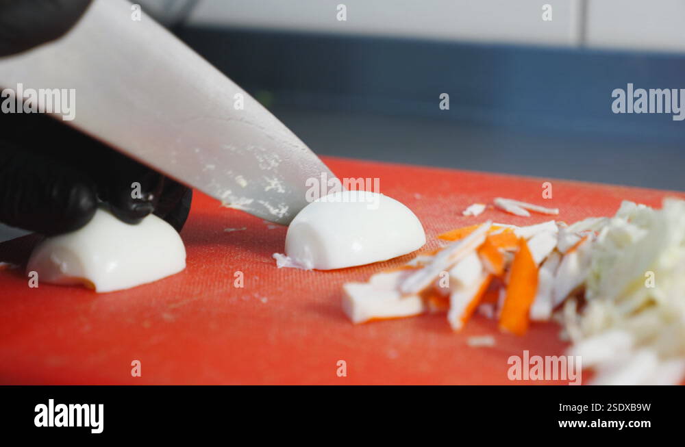 Hands of cook in gloves cutting a half boiled egg and slicing it using ...