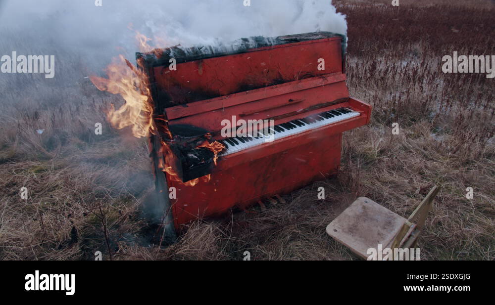 Burning red piano with a chair in a winter field during a snowfall ...