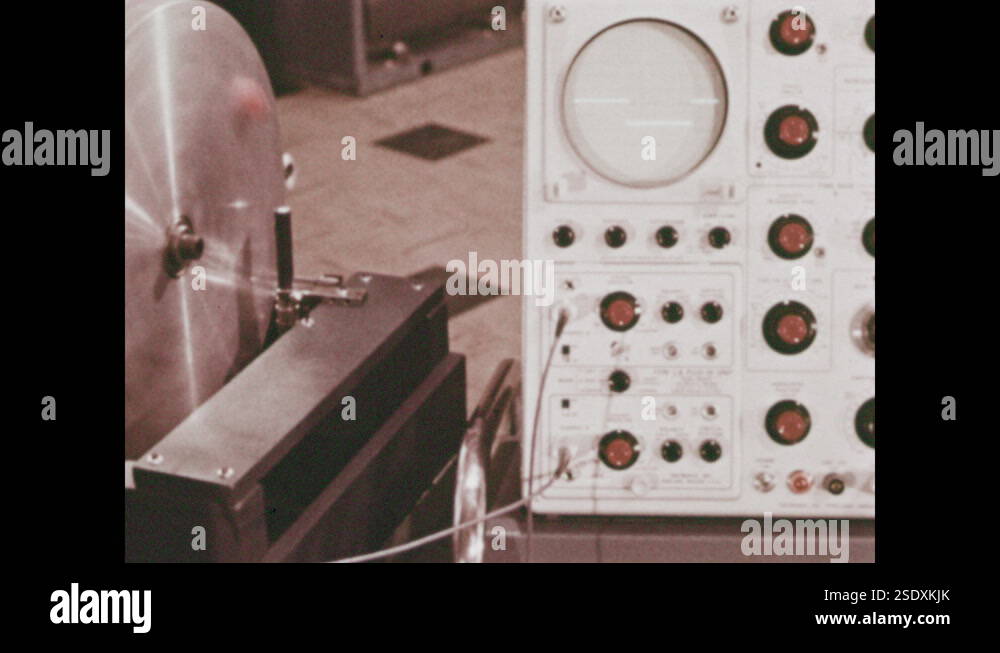 1970s: Drum rotates in lab next to control panel. Man in suit makes ...