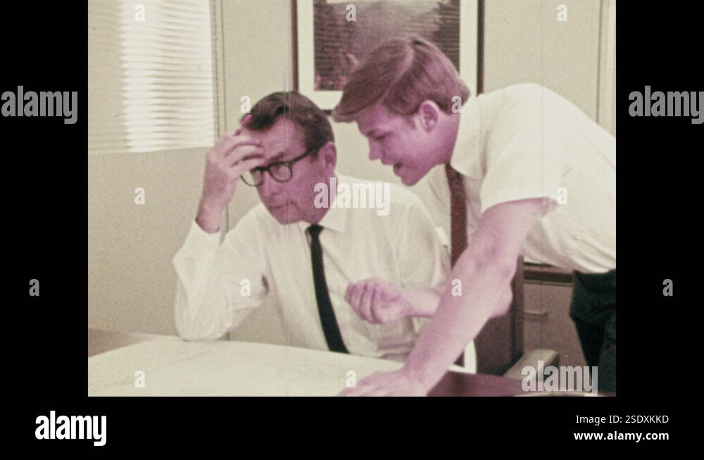 1970s: Office. Young man leans over annoyed boss as men review papers ...
