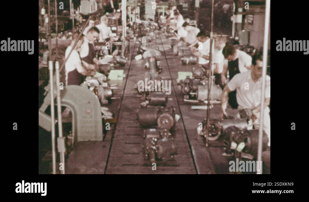 1970s: Workers assemble motors in factory. Worker hooks engine on ...