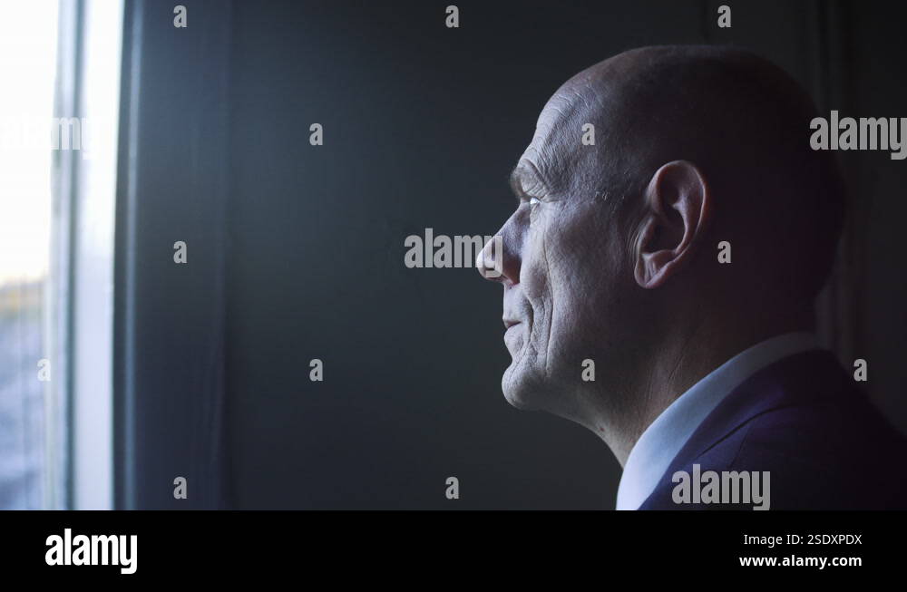 A lonely mature senior businessman stares out of a window in winter. He ...