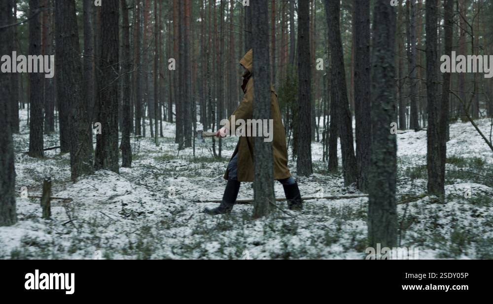 Scary man with a cape and an olde axe in hands walking in woods in ...