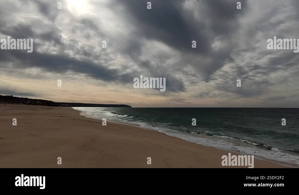 Dramatic wide shot of golden beach, ocean shore and hiding sun behind ...