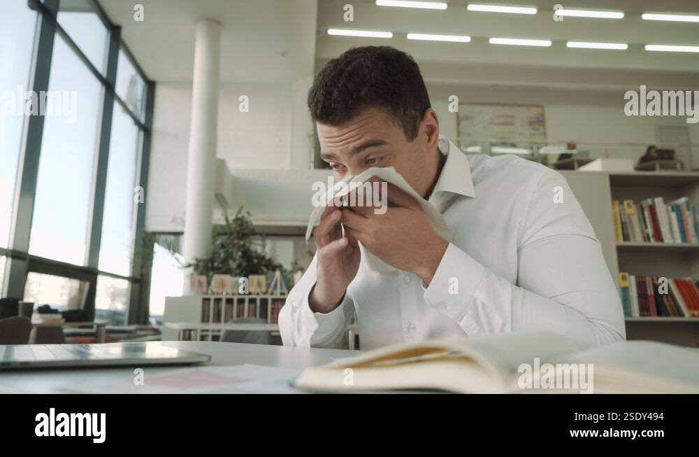 sick man in the office sneezes into a napkin at his desk, employee with ...
