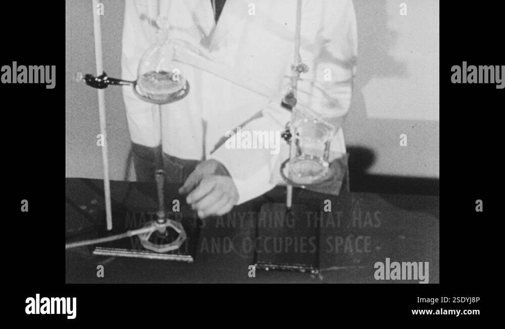 1960s: Man in lab stands near chemistry equipment. Man places weight on ...