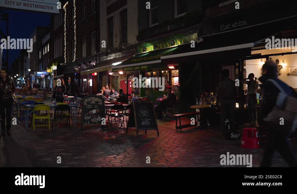 People sit outside a bar at night in London as others walk past during ...