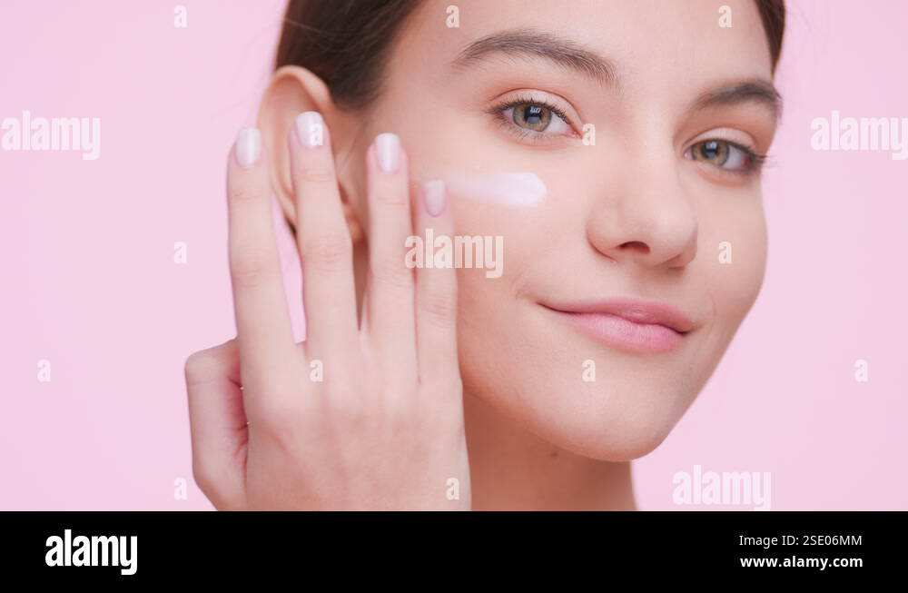 Beauty model applies cream on her face and looks at the camera Stock ...